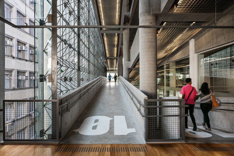 A modern indoor walkway with large glass windows and concrete walls ...
